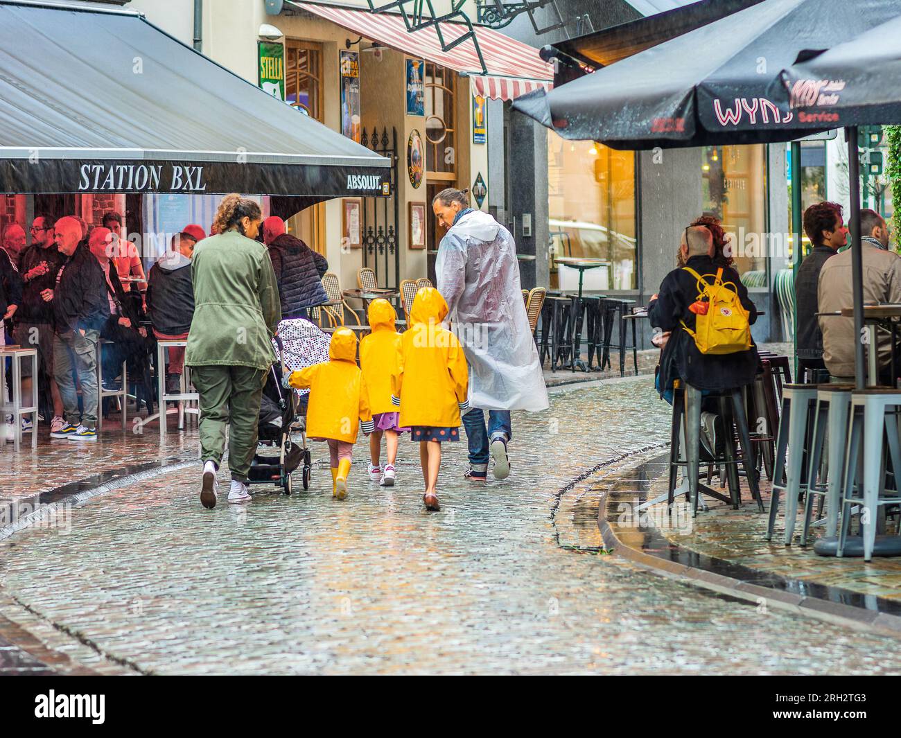 Family with children in yellow rain macs walking along street during ...