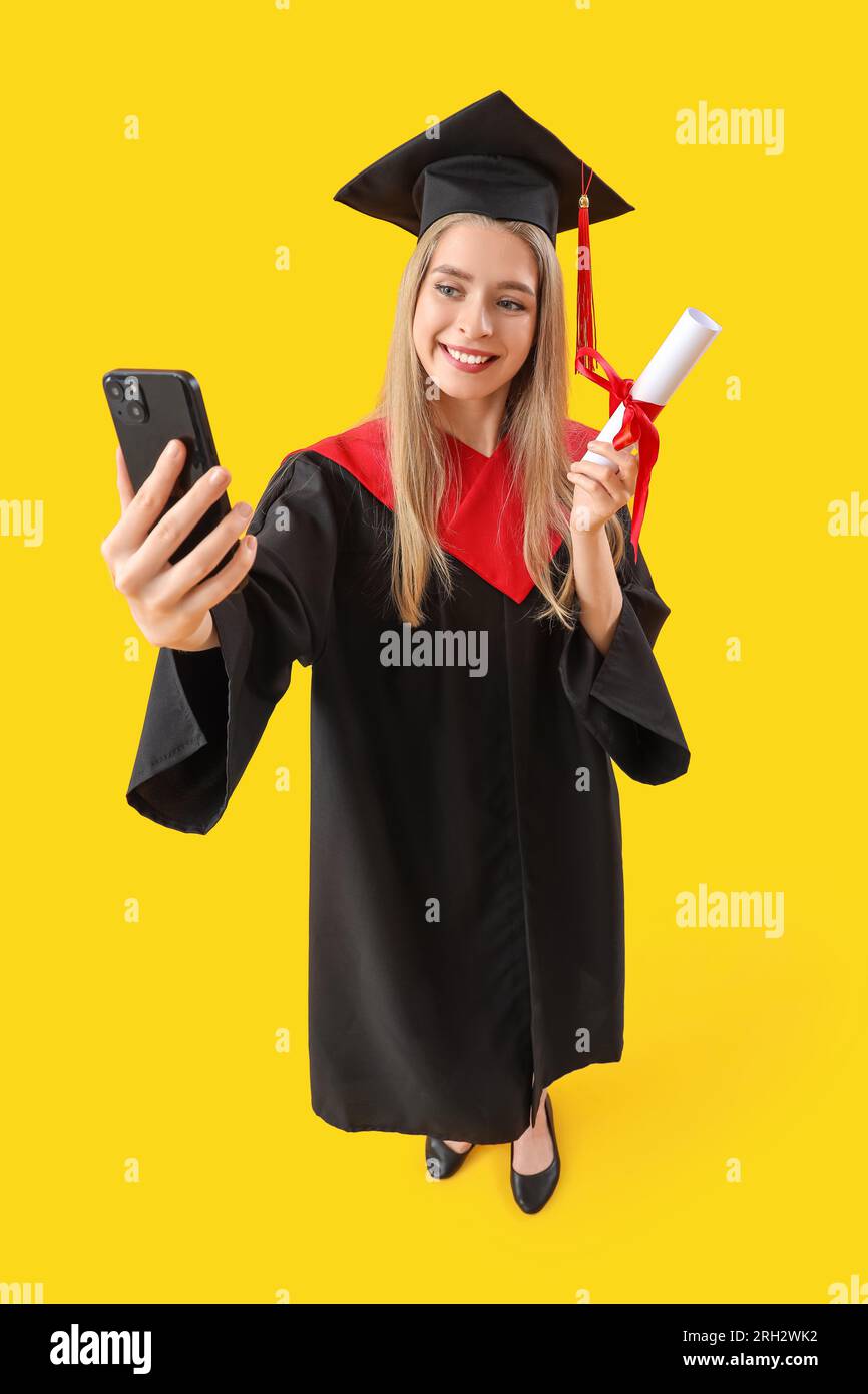 Female graduate student with diploma taking selfie on yellow background ...
