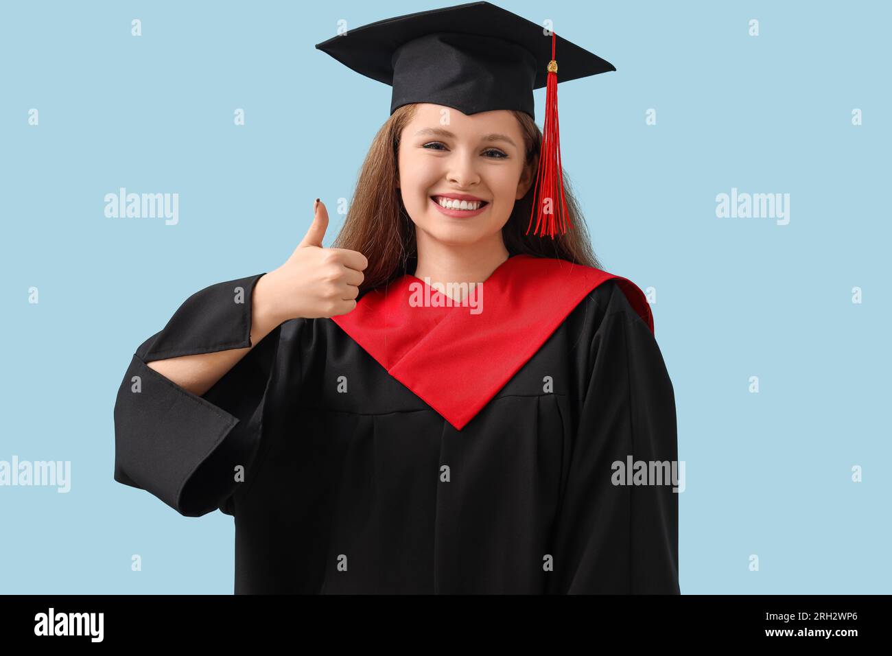Female graduate student showing thumb-up on blue background Stock Photo ...