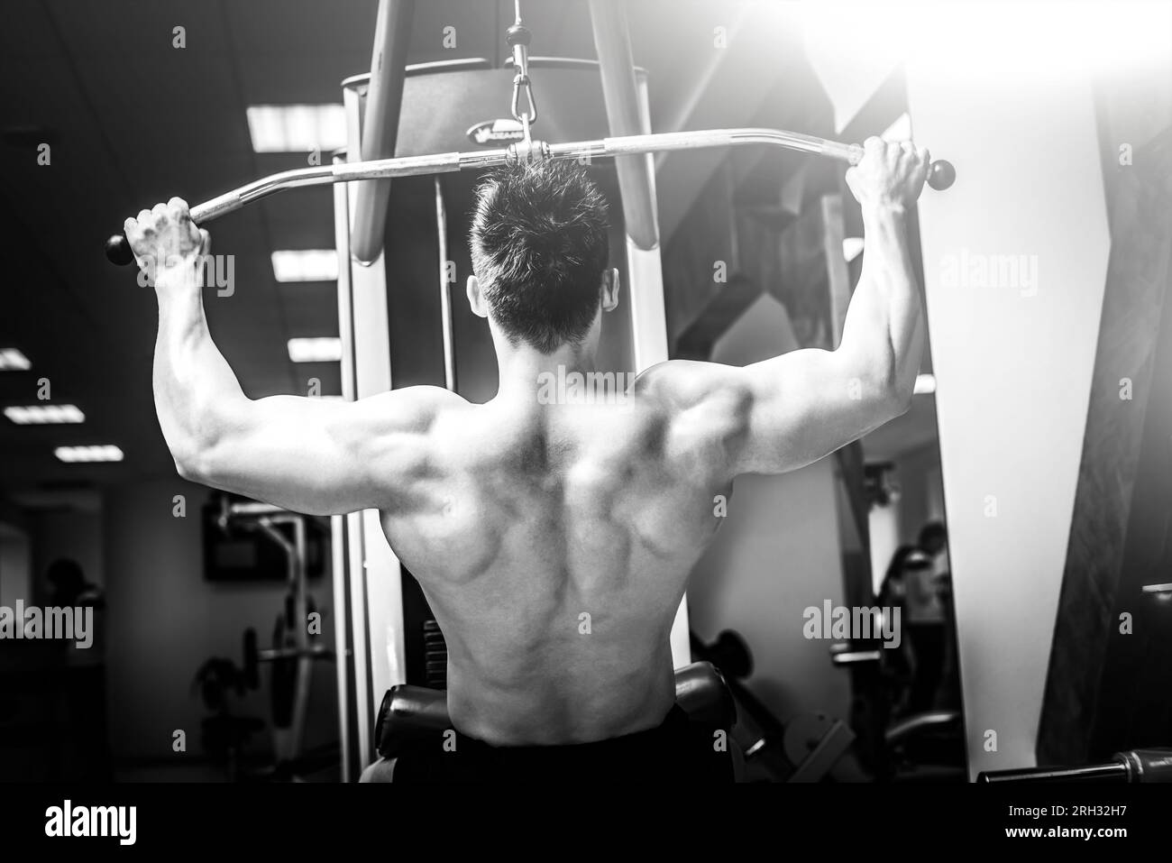 Strong bodybuilder man pulling a vertical upper block in a modern gym ...