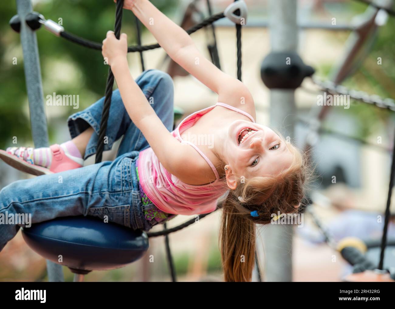 Funny smiling little girl playing at the playground and climb the ropes ...