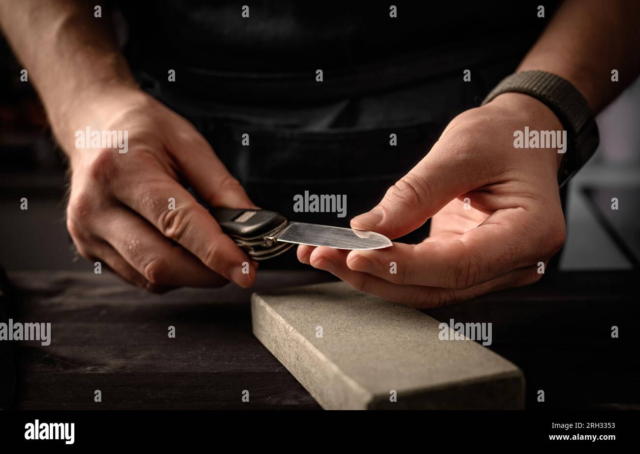 Man's hands with folding knife and sharpen stone tool. master ...