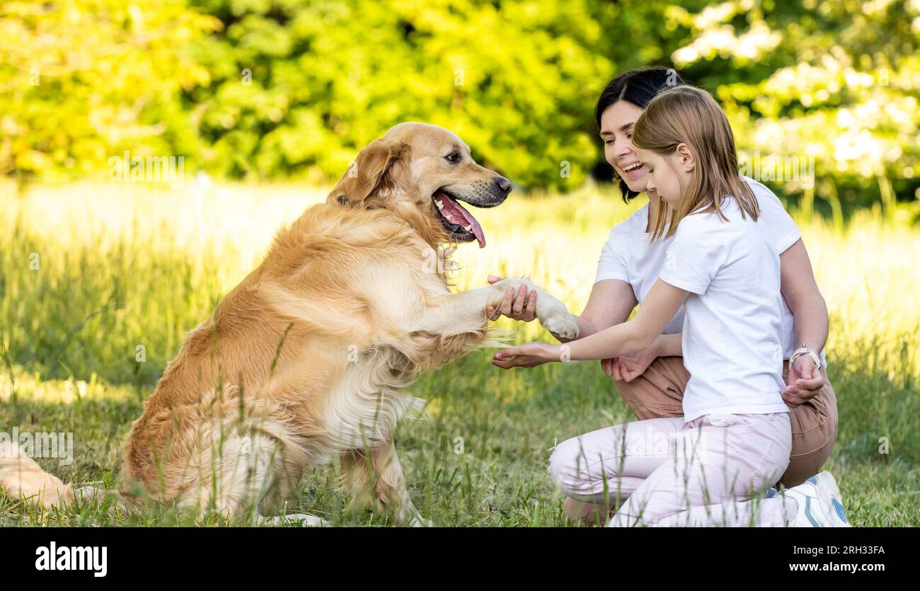 Mother and cute daughter playing with adorable golden retriever dog outdoors Stock Photo - Alamy