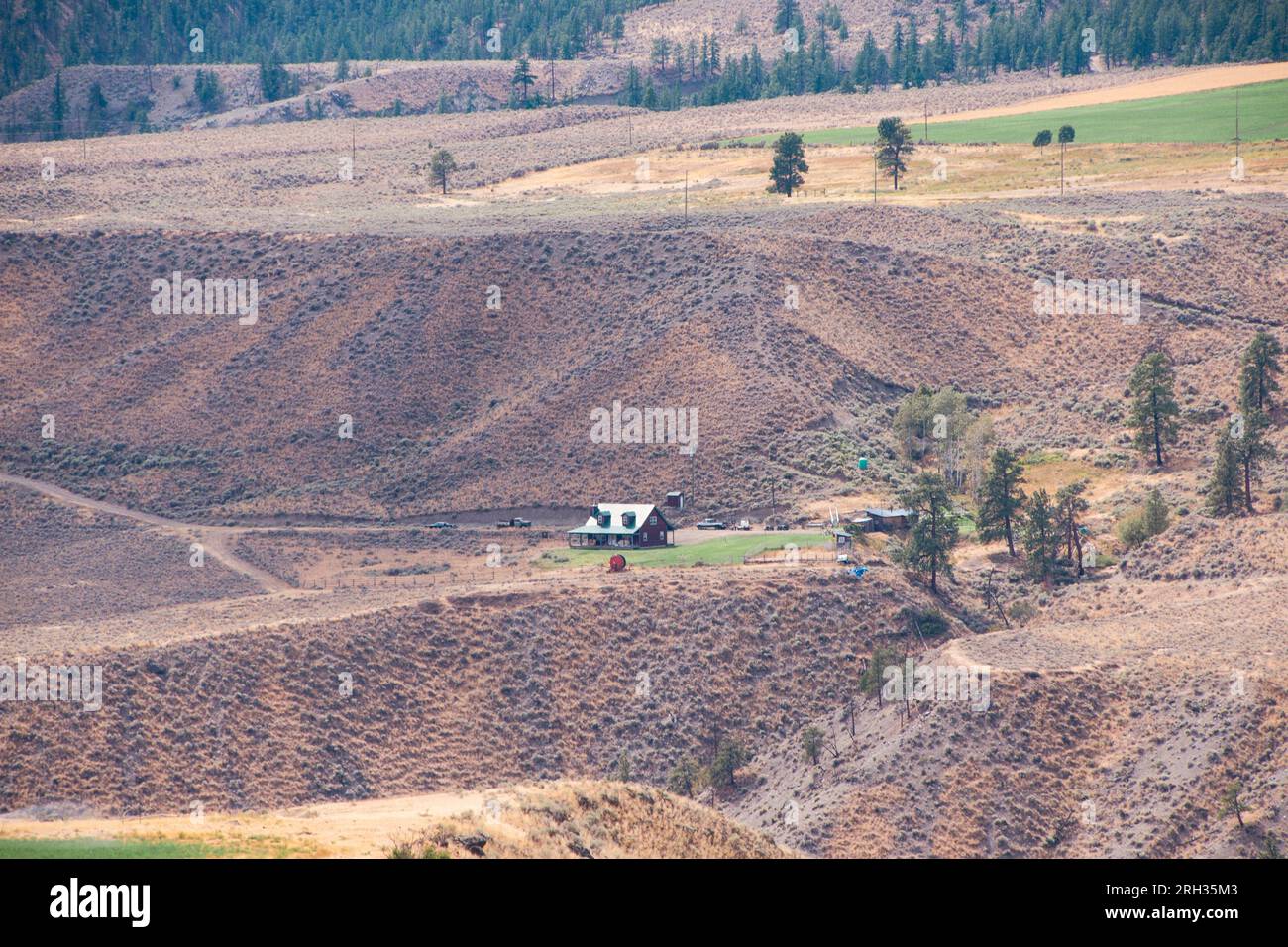 A farm house in the middle of an empty field surrounded by small hills ...