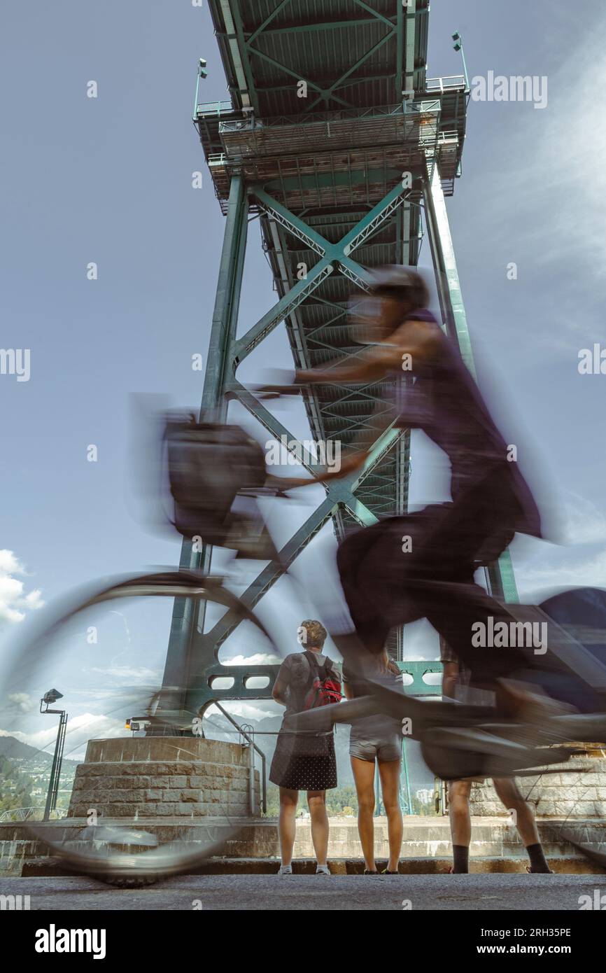 A cyclist rides passed some tourists under Lions Gate Bridge in ...