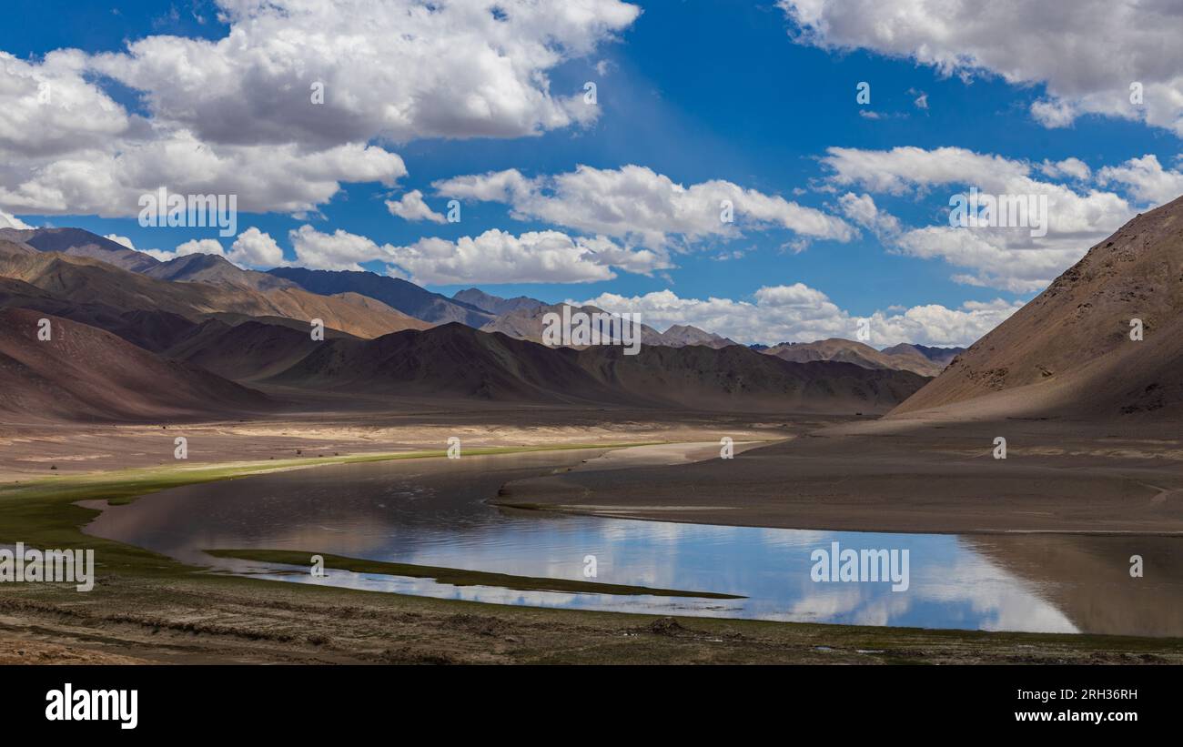 An open valley in Ladakh with a river flowing in the center and clouds ...