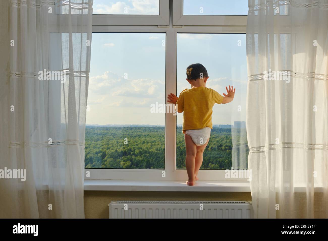 The child is precariously perched on the window sill, looking out the ...