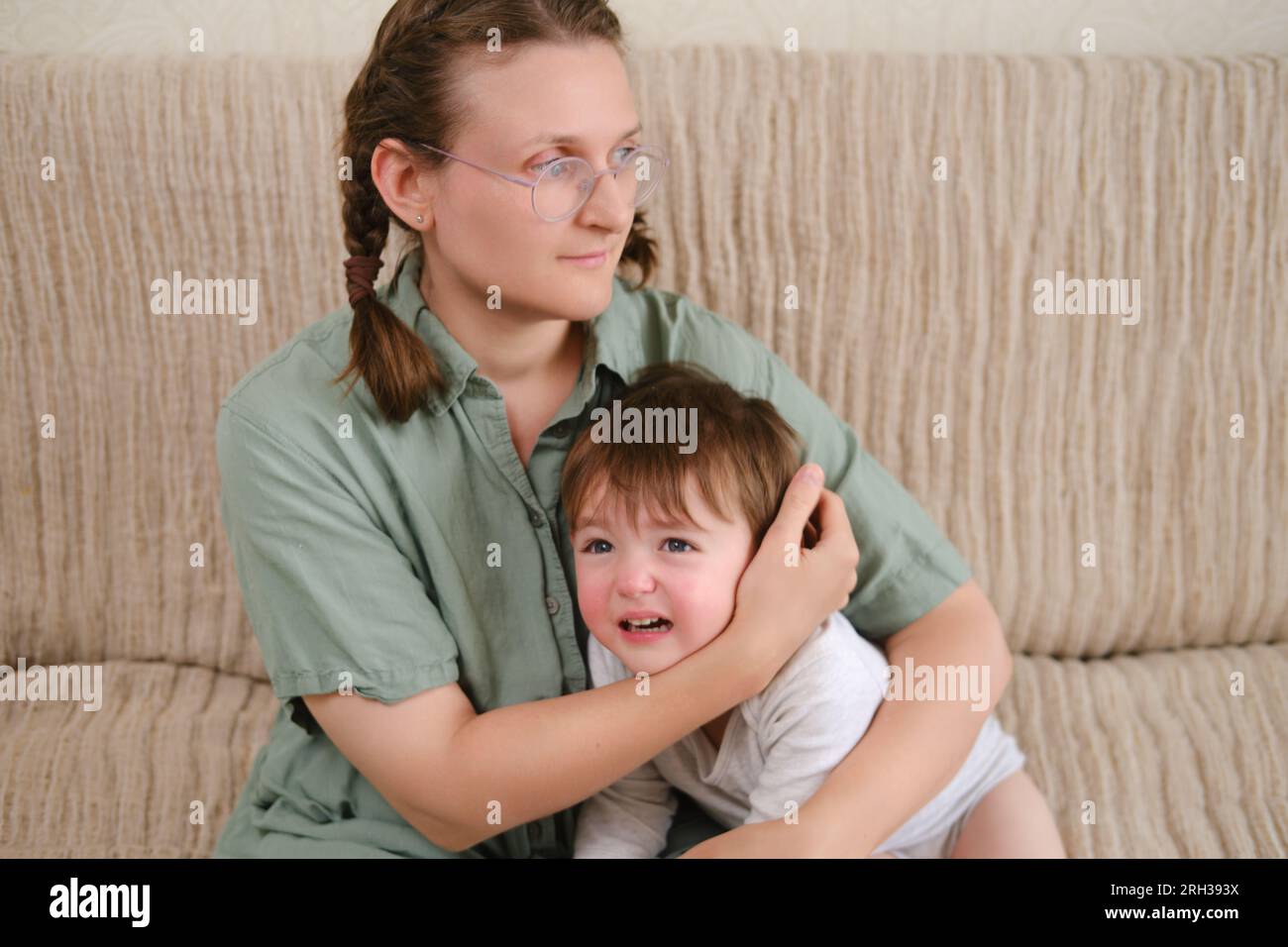 Portrait of an adult woman with a crying baby sitting on a sofa, female ...