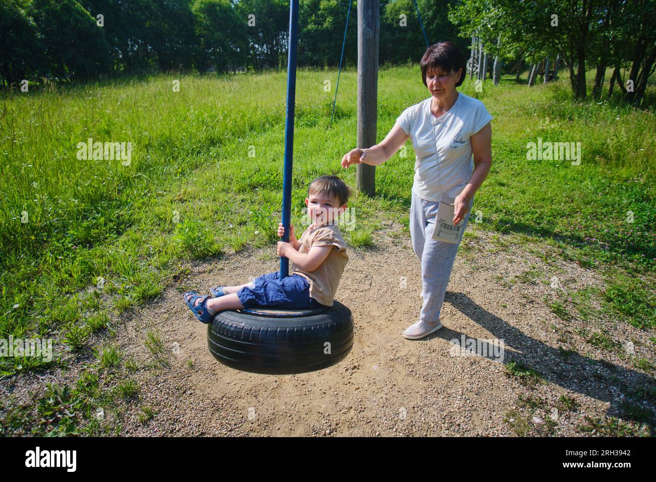 Grandma rides baby on a tire from a car wheel that has turned into a ...