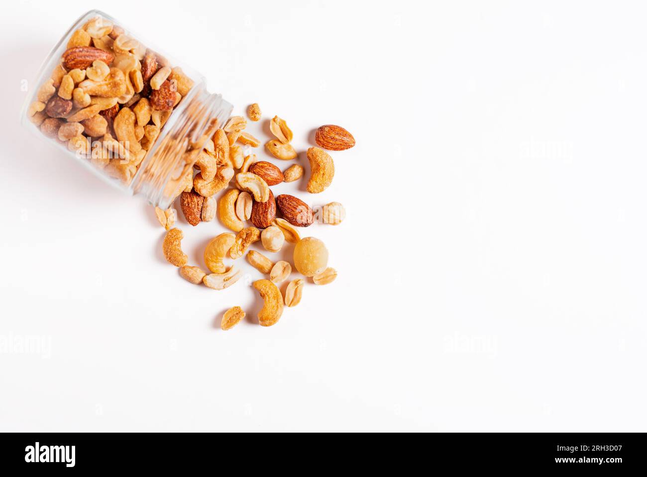 Glass jar lying down with a mix of roasted nuts spilling out from ...