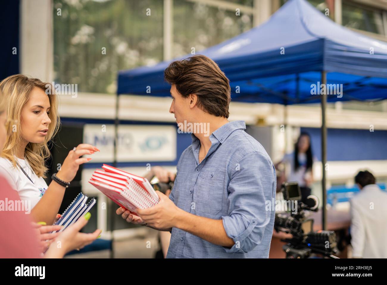 Lovely female student taking a red notebook for her friend from her ...