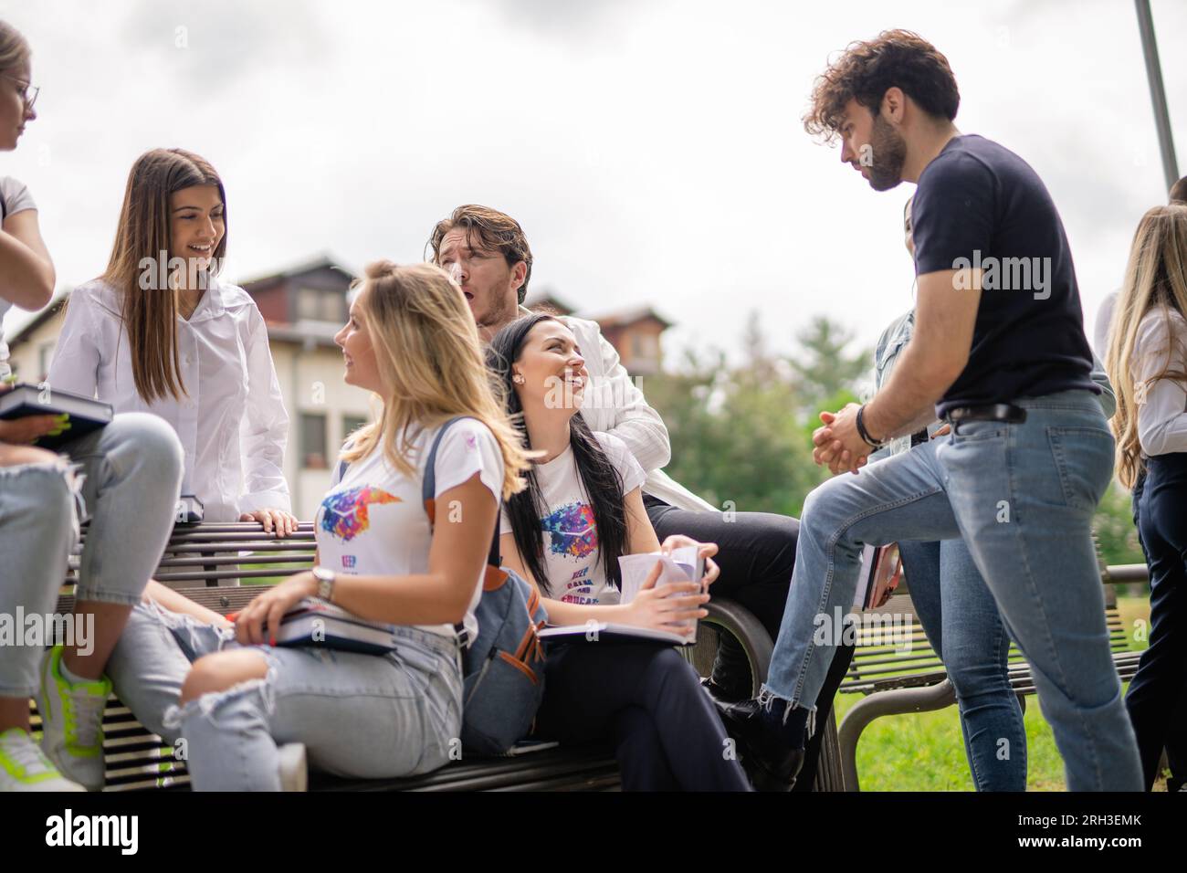 Young, happy, college students having a conversation sitting on a bench ...