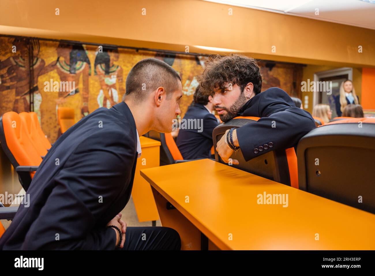 Two male students talking in class while attending a lecture Stock ...