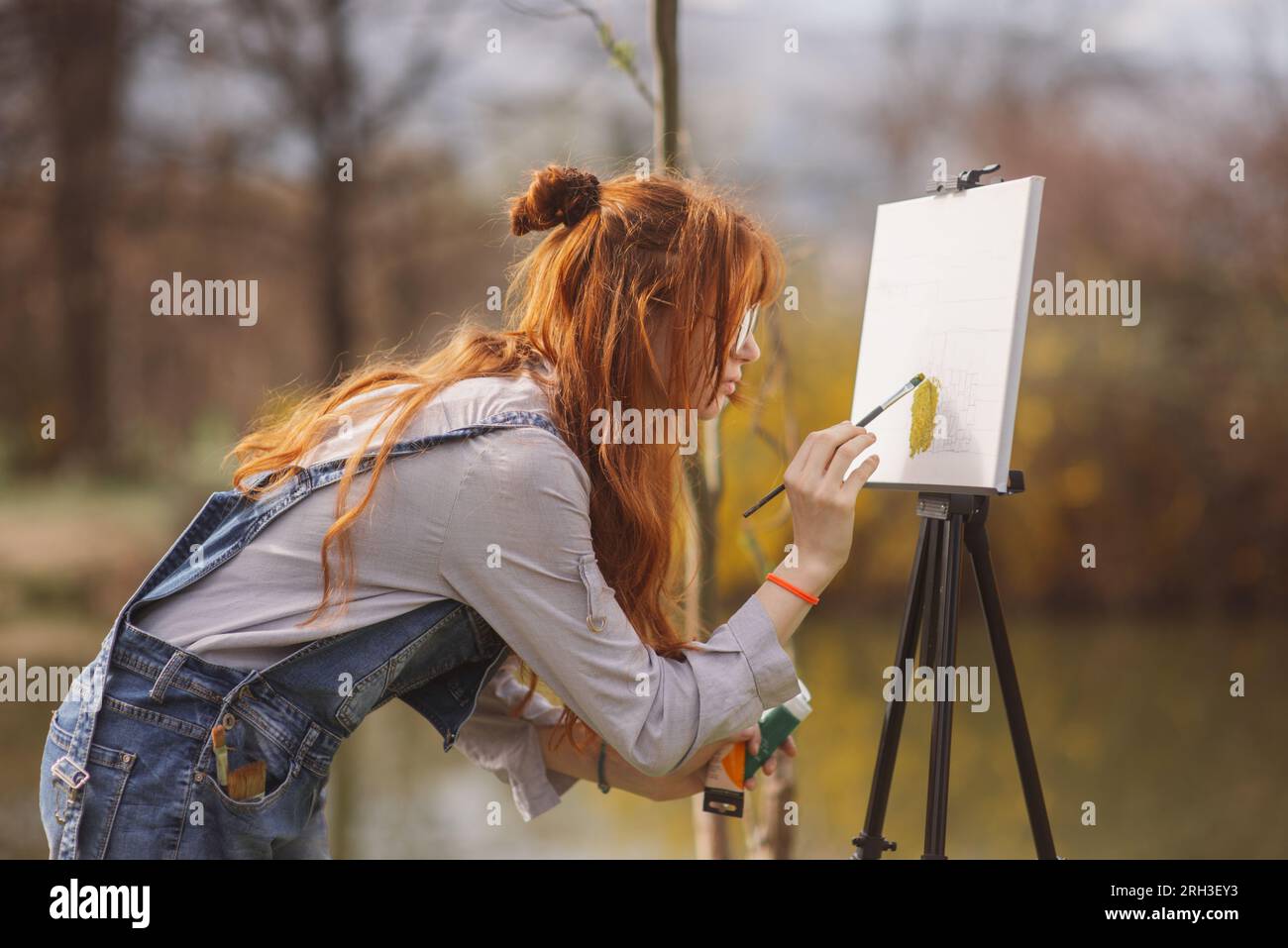 Beautiful female artist with red hair is painting on a easel while ...