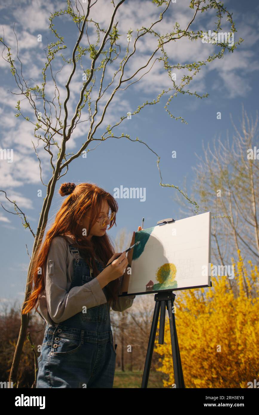 Beautiful ginger girl is painting on a canvas with her color palette ...