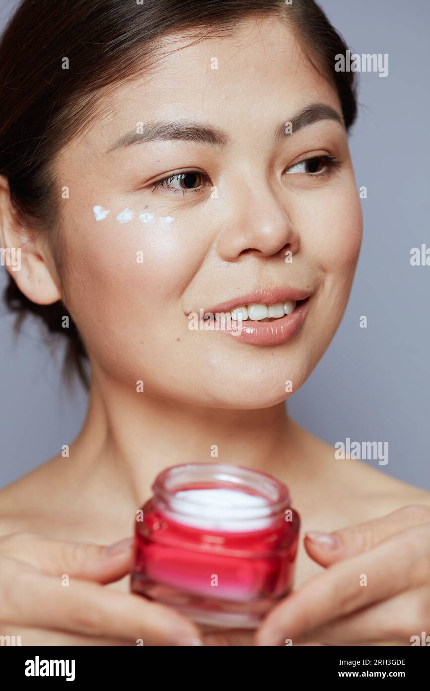 young woman with facial cream jar and eye cream on face against blue background Stock Photo - Alamy