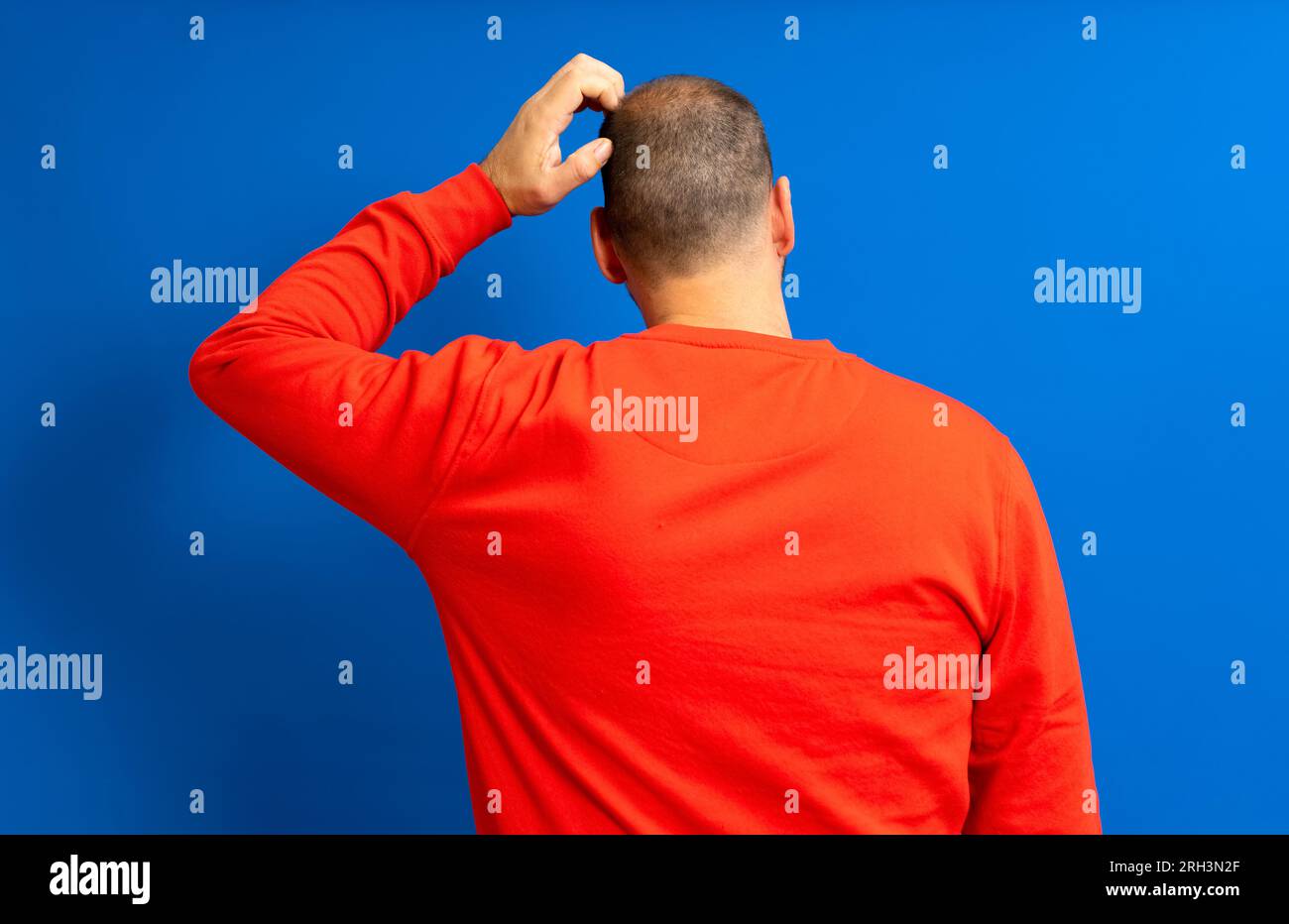 Back view of thoughtful man scratching his head over blue background ...