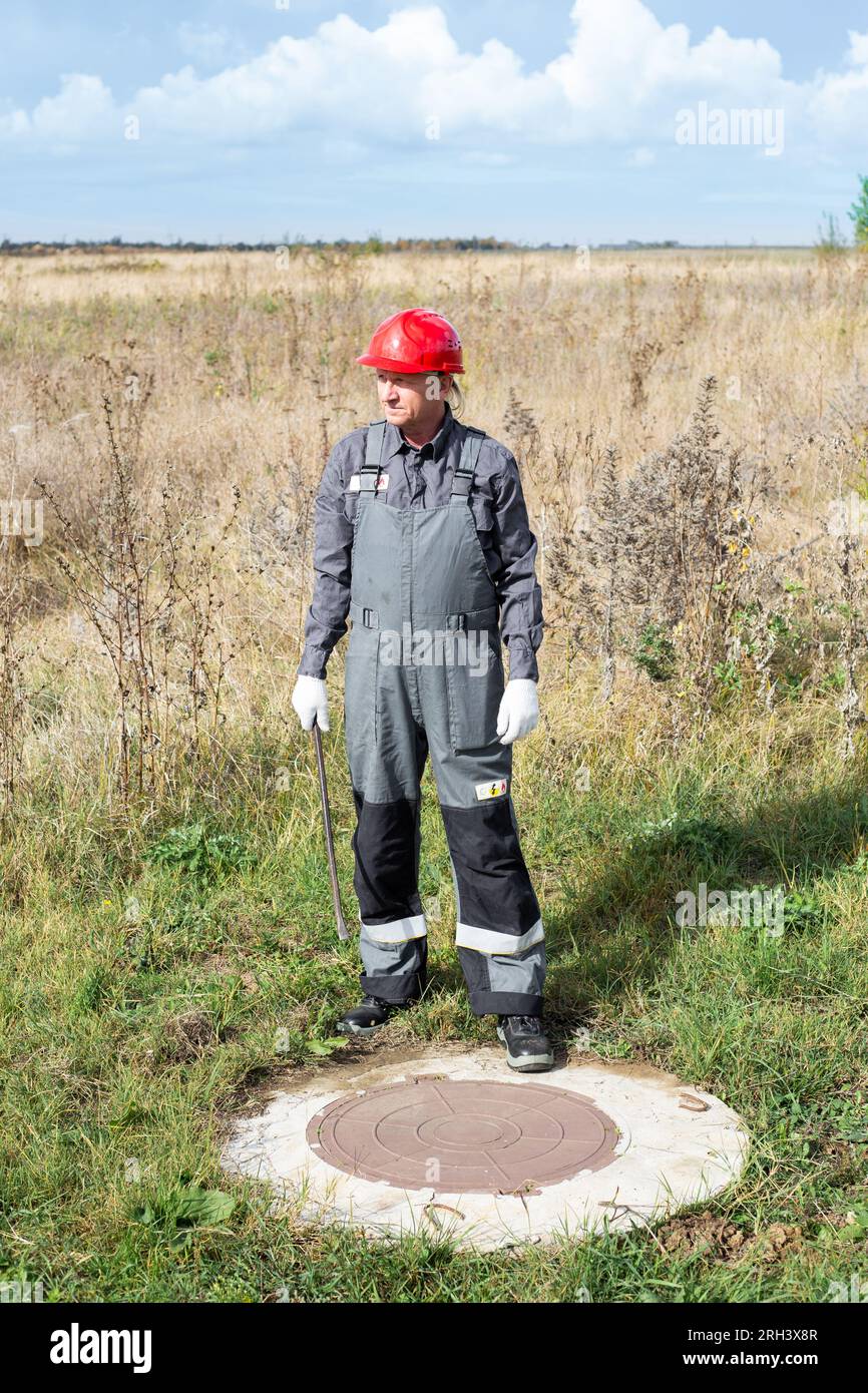 A worker in overalls and a helmet near a manhole. Control and ...