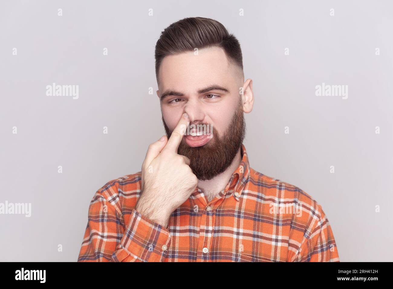 Mischievous bearded man putting finger into his nose and showing tongue ...