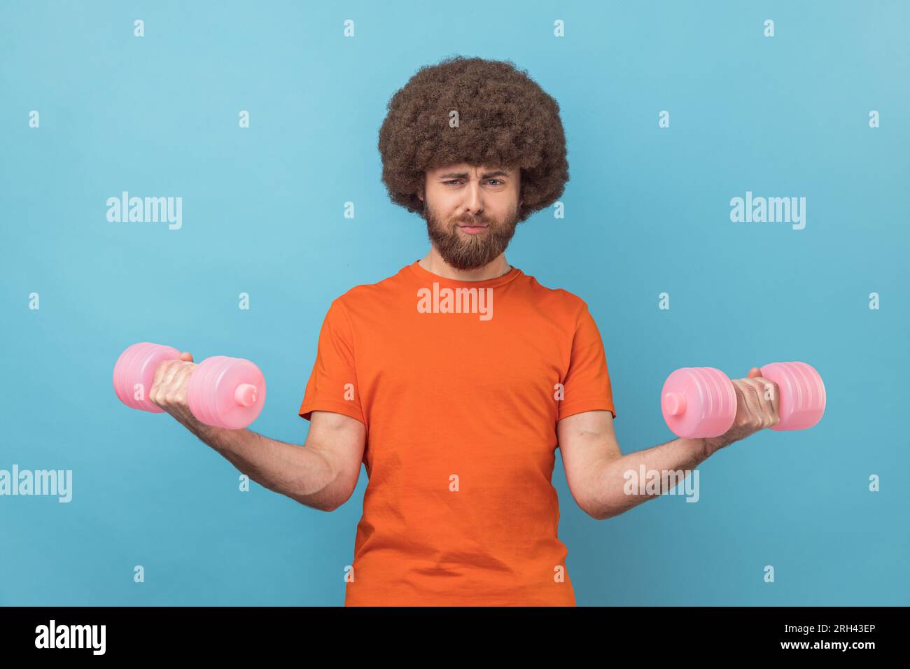 Portrait of funny man with Afro hairstyle wearing orange T-shirt rising ...