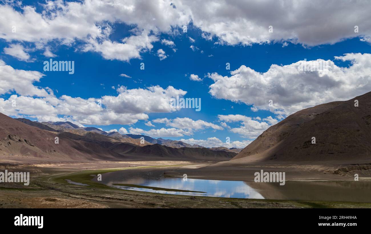 An open valley in Ladakh with a river flowing in the center and clouds ...