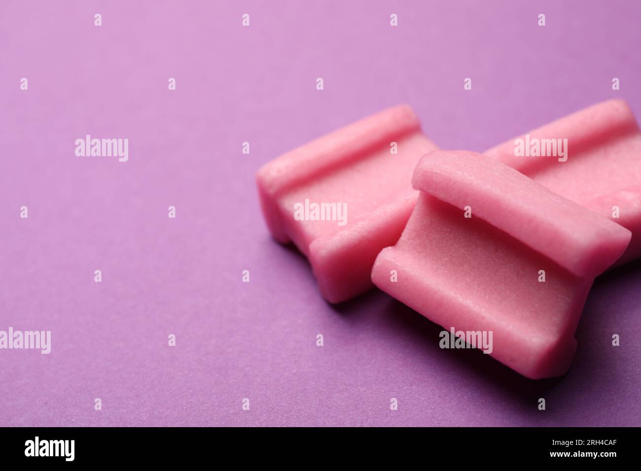 Tasty pink chewing gums on purple background, closeup. Space for text ...