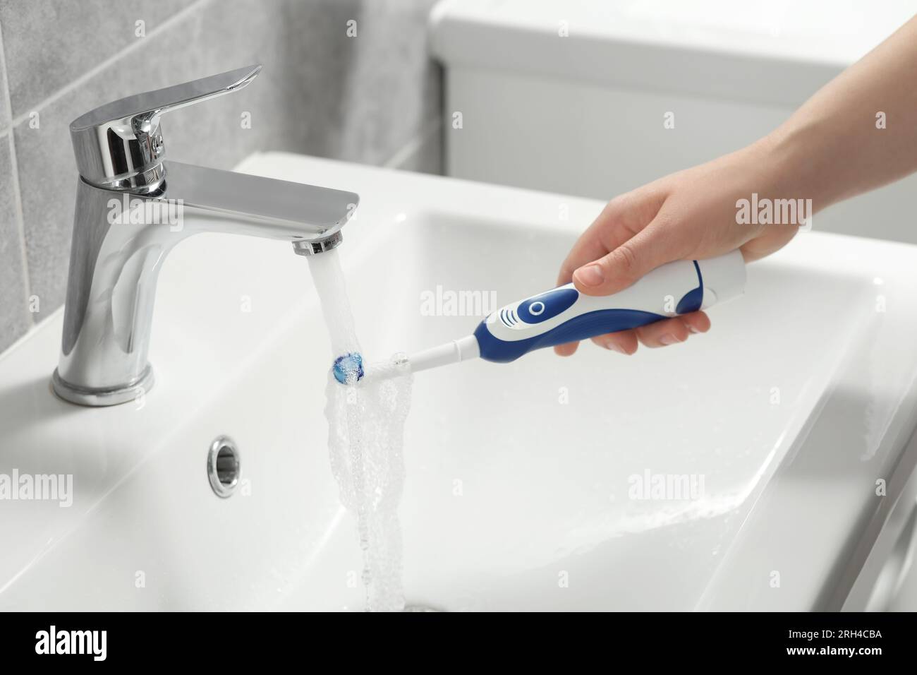 Woman washing electric toothbrush under flowing water from faucet in ...
