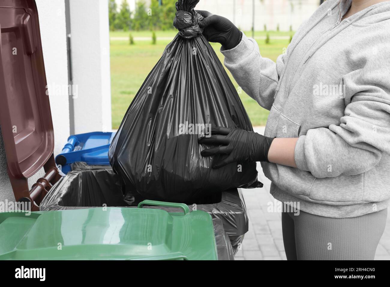 Woman throwing trash bag full of garbage in bin outdoors, closeup ...