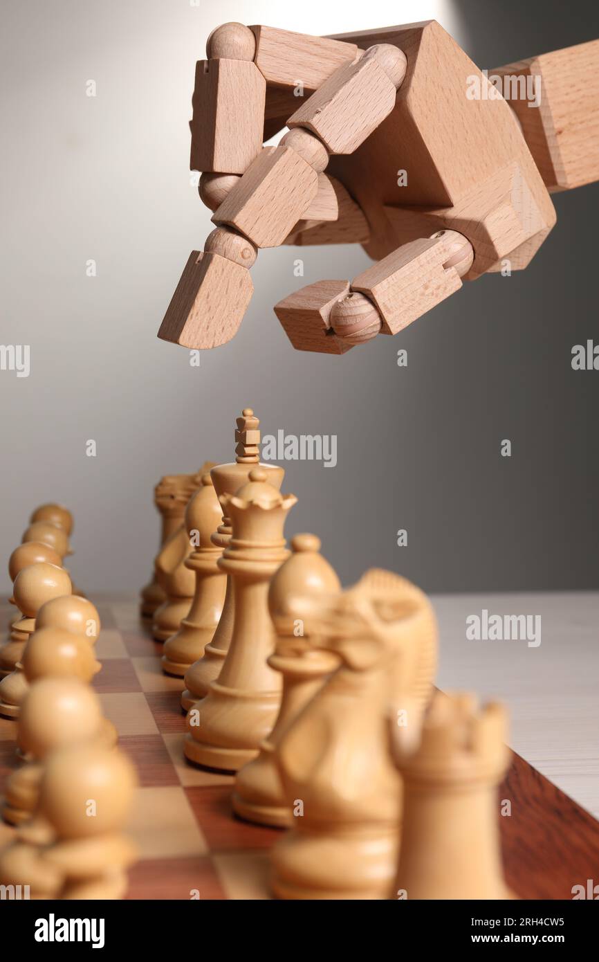 Robot playing chess against light grey background, closeup. Wooden hand ...