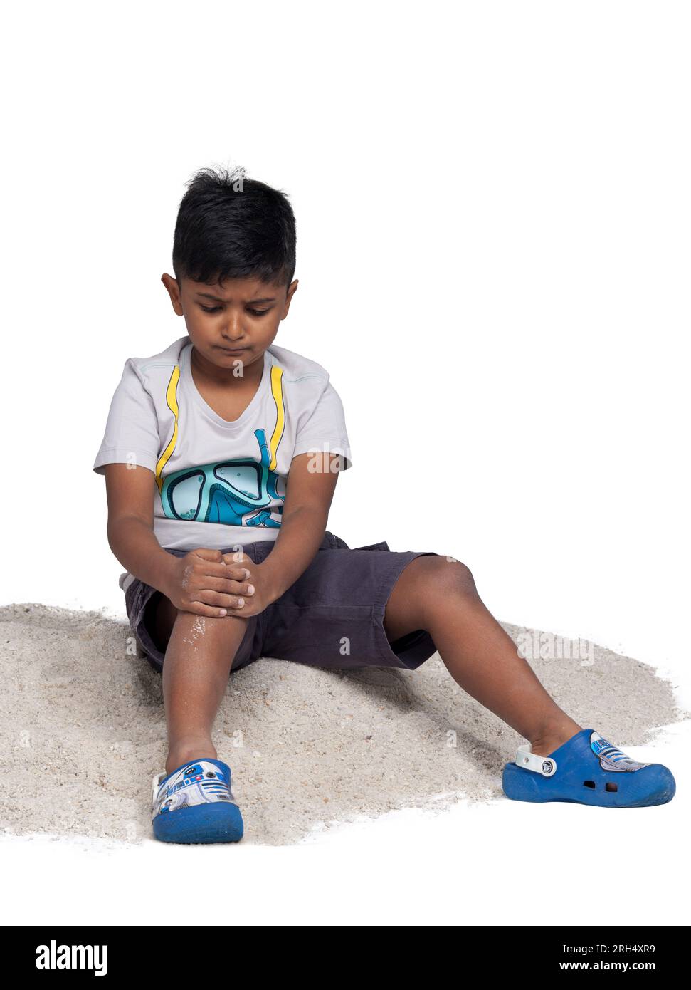 Physically injured indian boy holding his knee area sitting on sand in ...