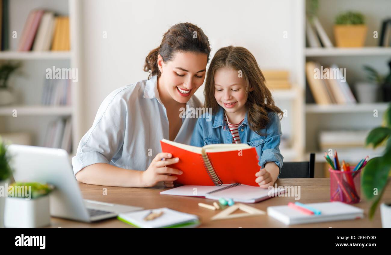 Happy child and adult are sitting at desk. Girl doing homework or ...