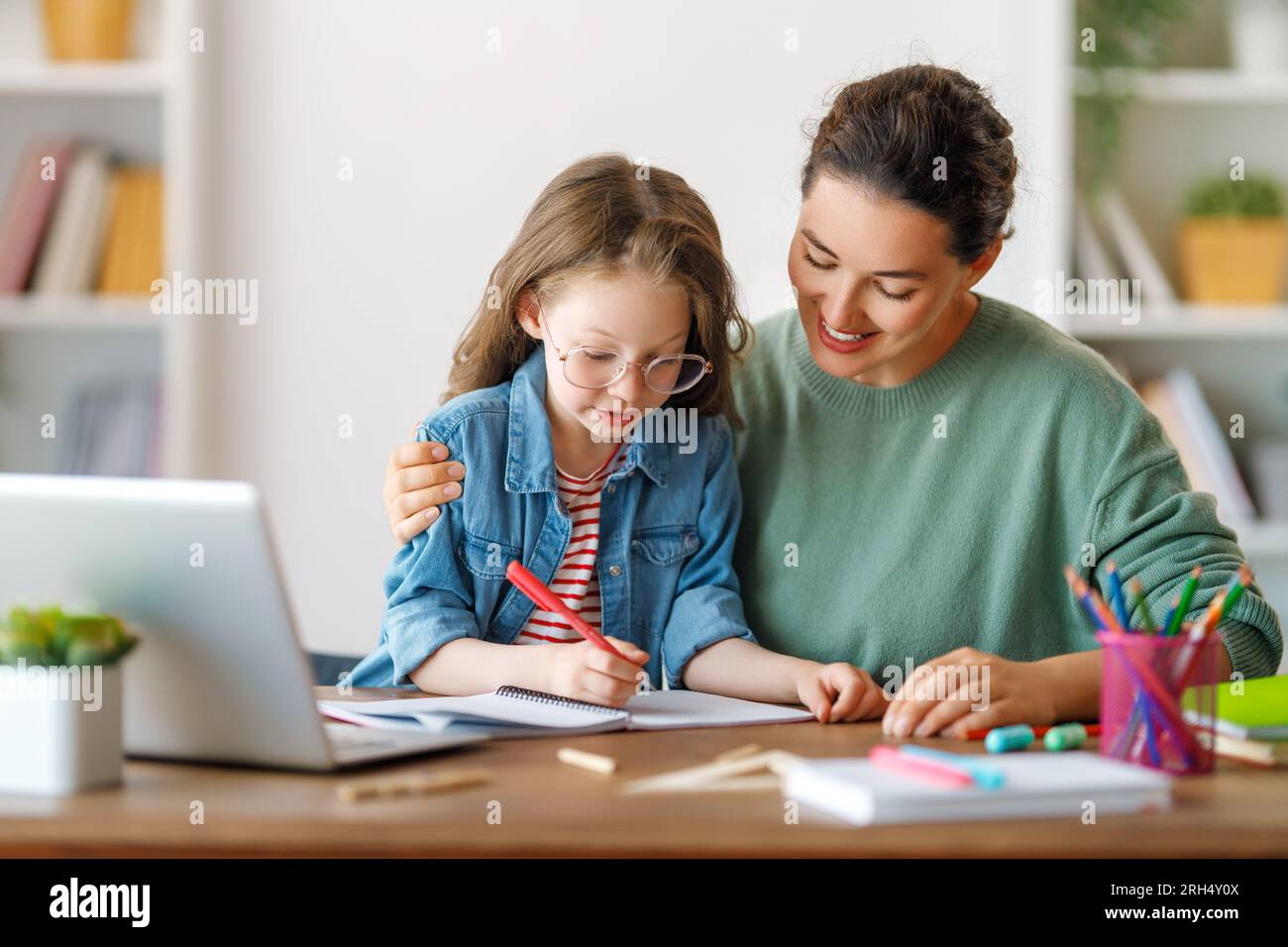 Happy child and adult are sitting at desk. Girl doing homework or ...