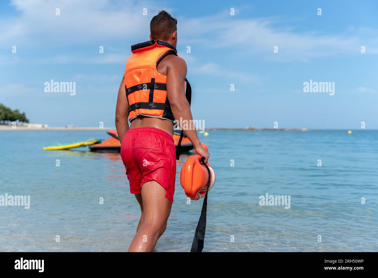Rear view of a lifeguard with float gazing the ocean ready for an ...