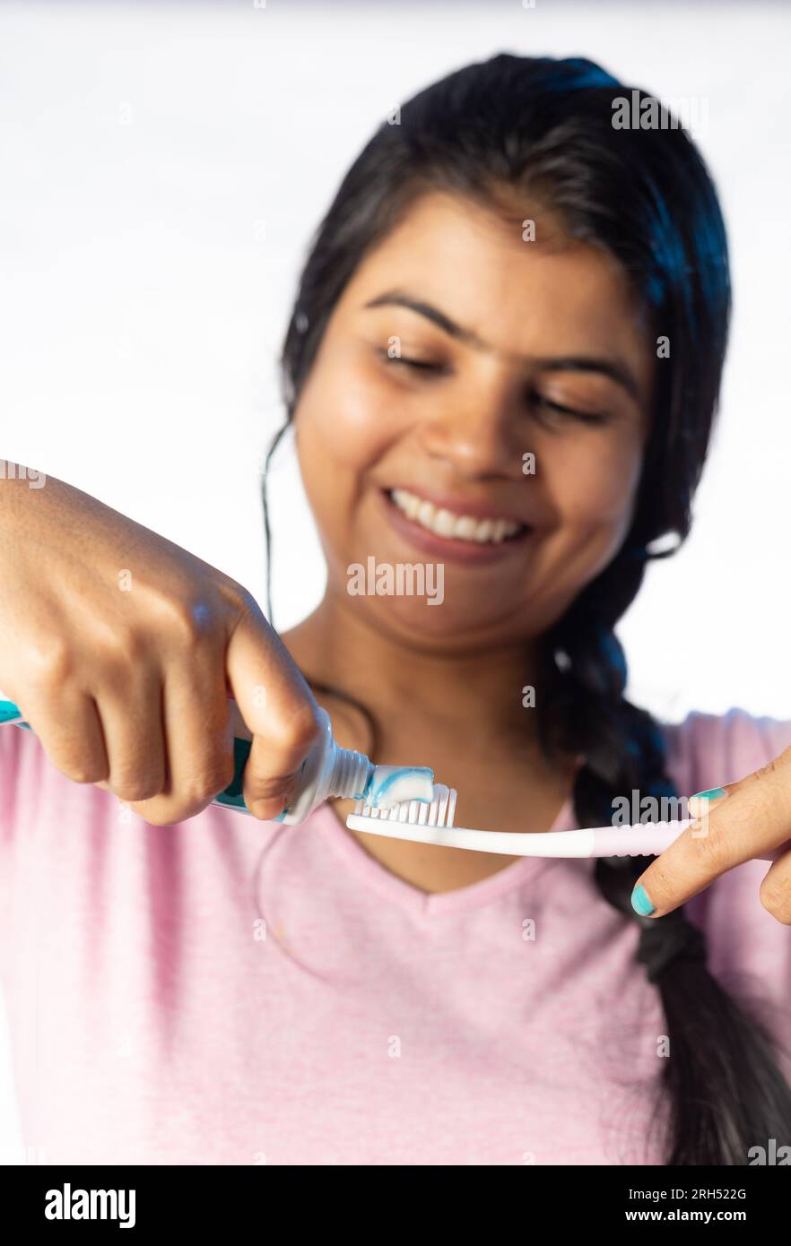 An Indian woman female girl applying toothpaste on toothbrush on white ...