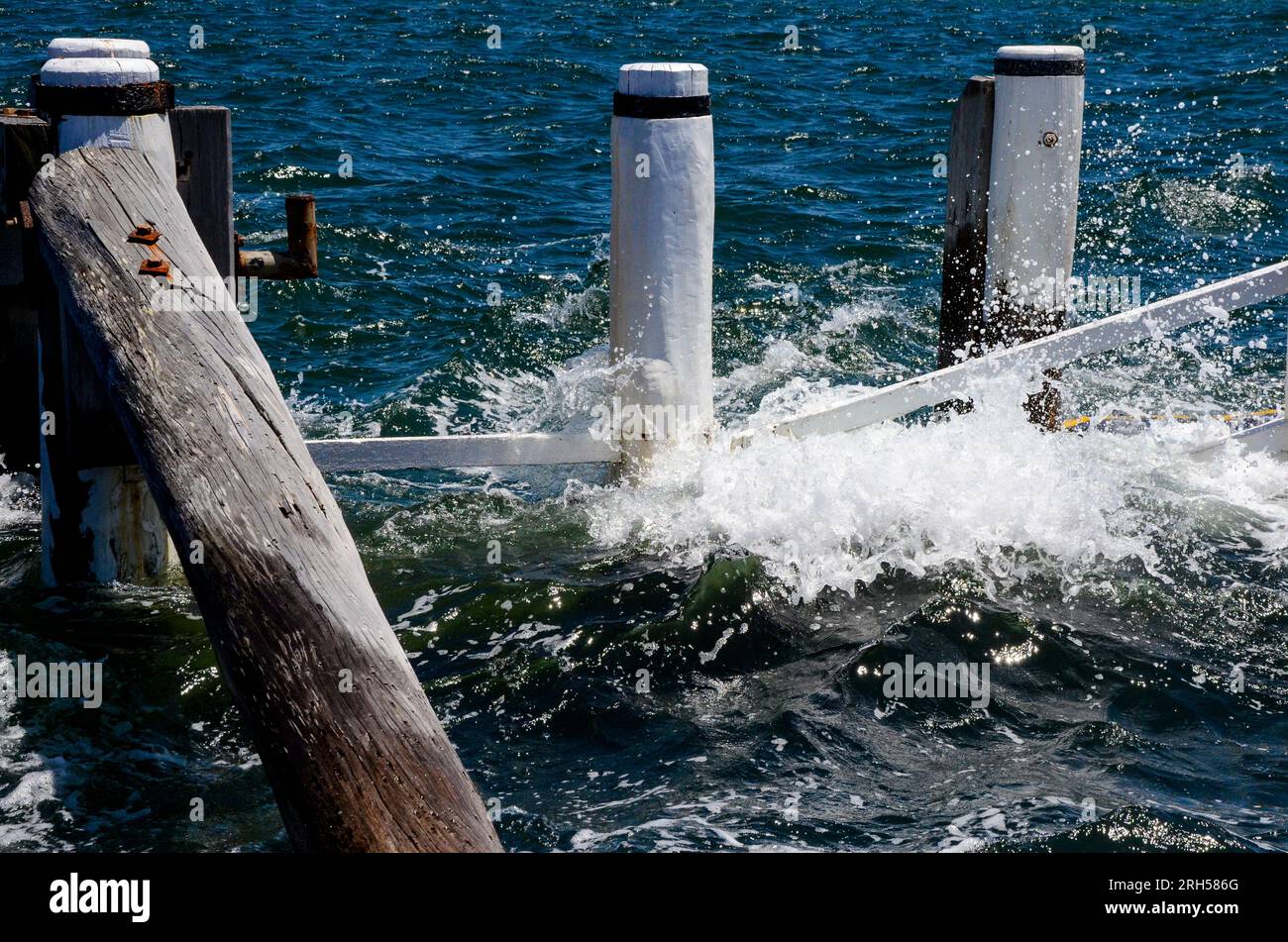 Water splashing against wooden pier submerged in deep green blue water ...