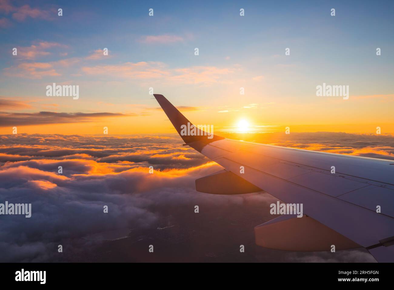 Airplane flight in sunset sky over ocean water and wing of plane. View ...