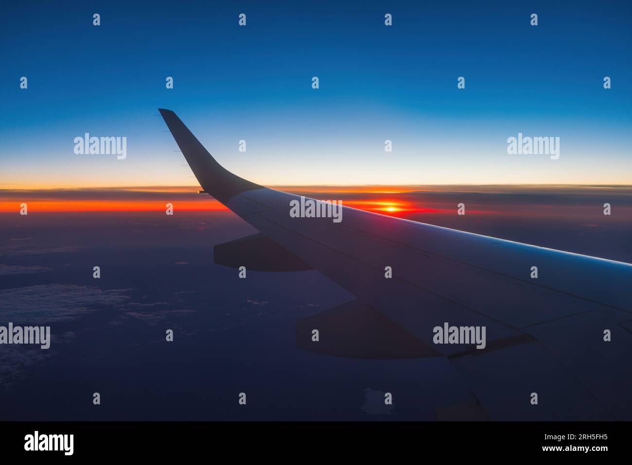 Airplane flight in sunset sky over ocean water and wing of plane. View ...