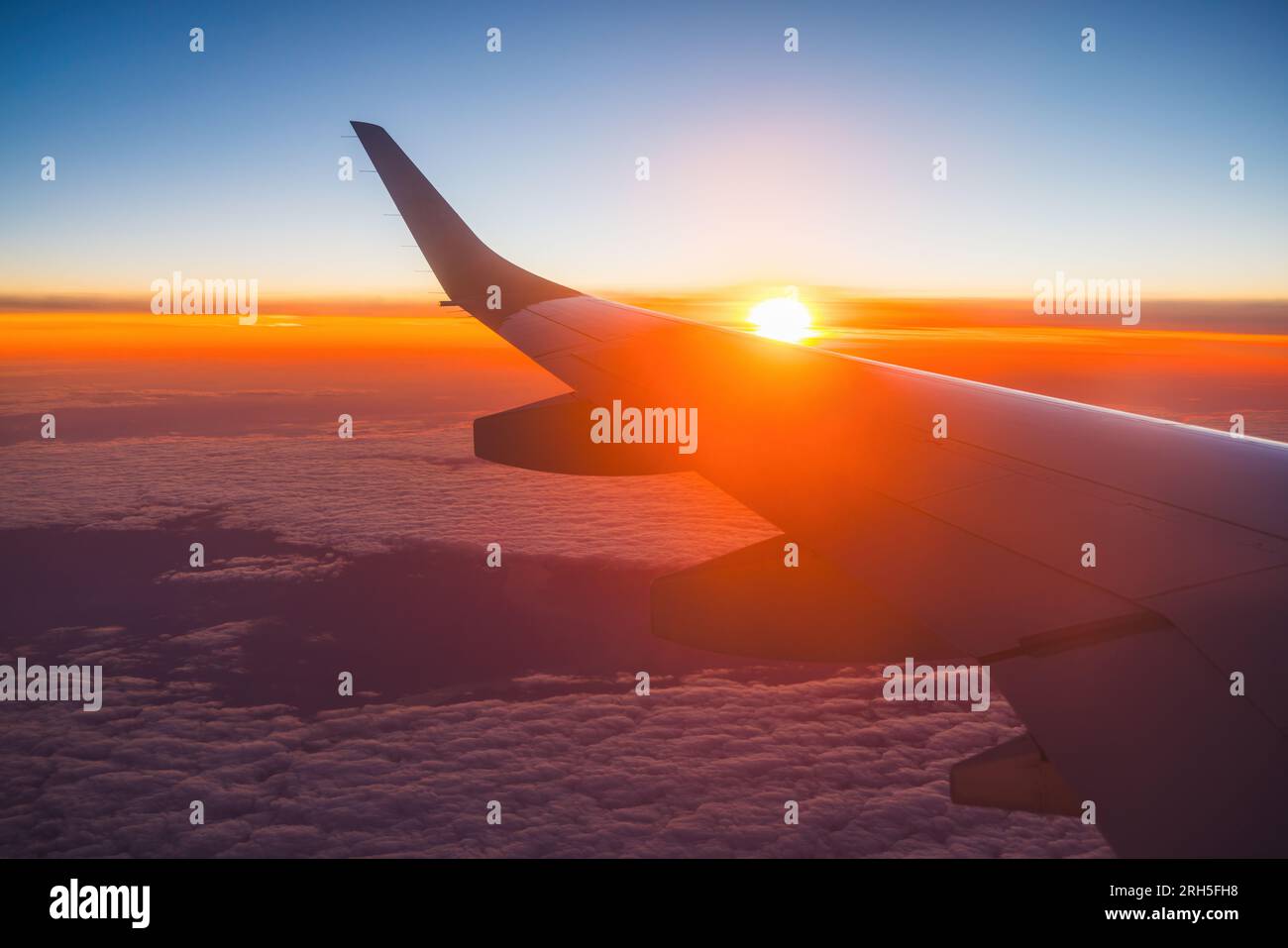 Airplane flight in sunset sky over ocean water and wing of plane. View ...