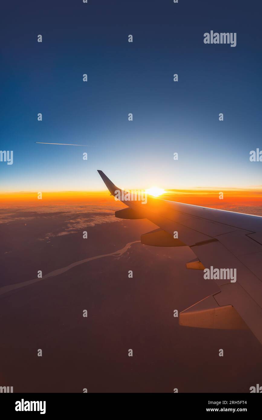 Airplane flight in sunset sky over ocean water and wing of plane. View ...