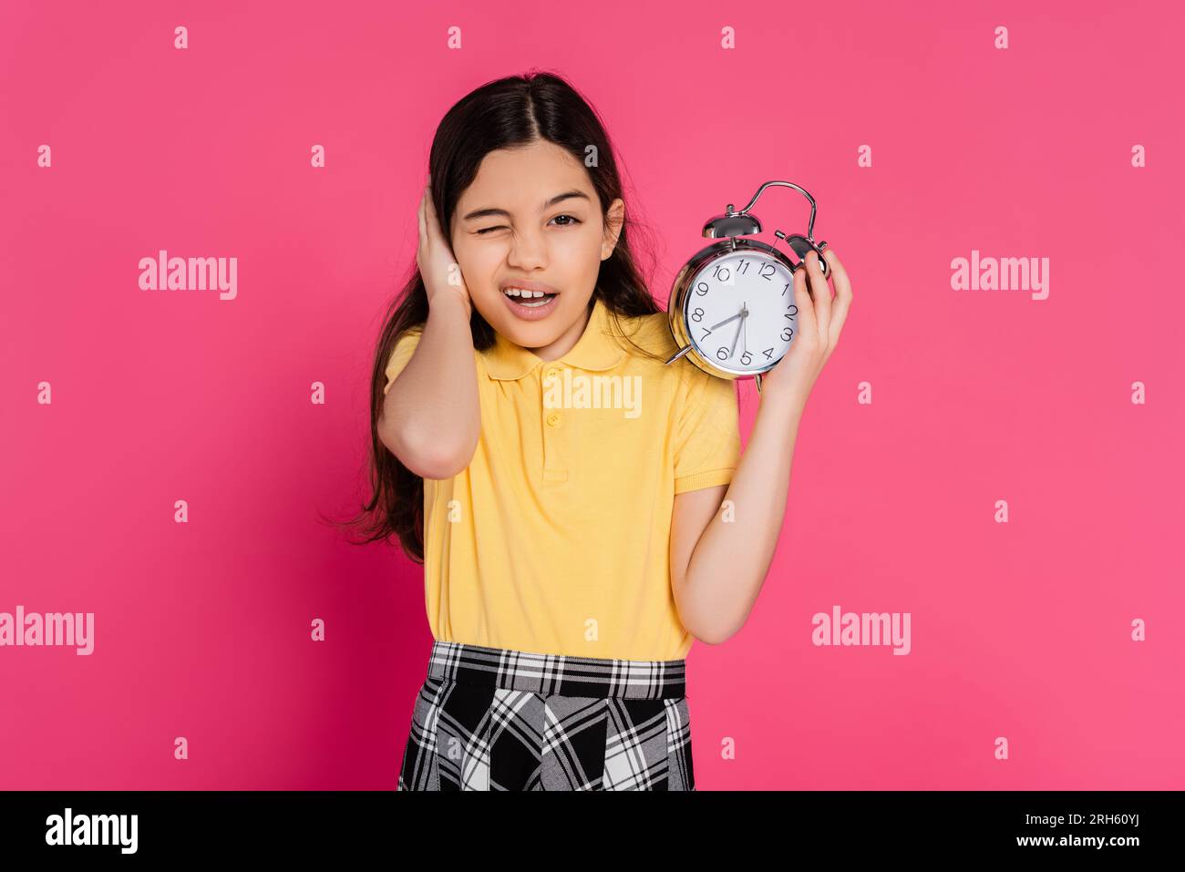 schoolgirl looking at camera, winking, holding vintage alarm clock ...