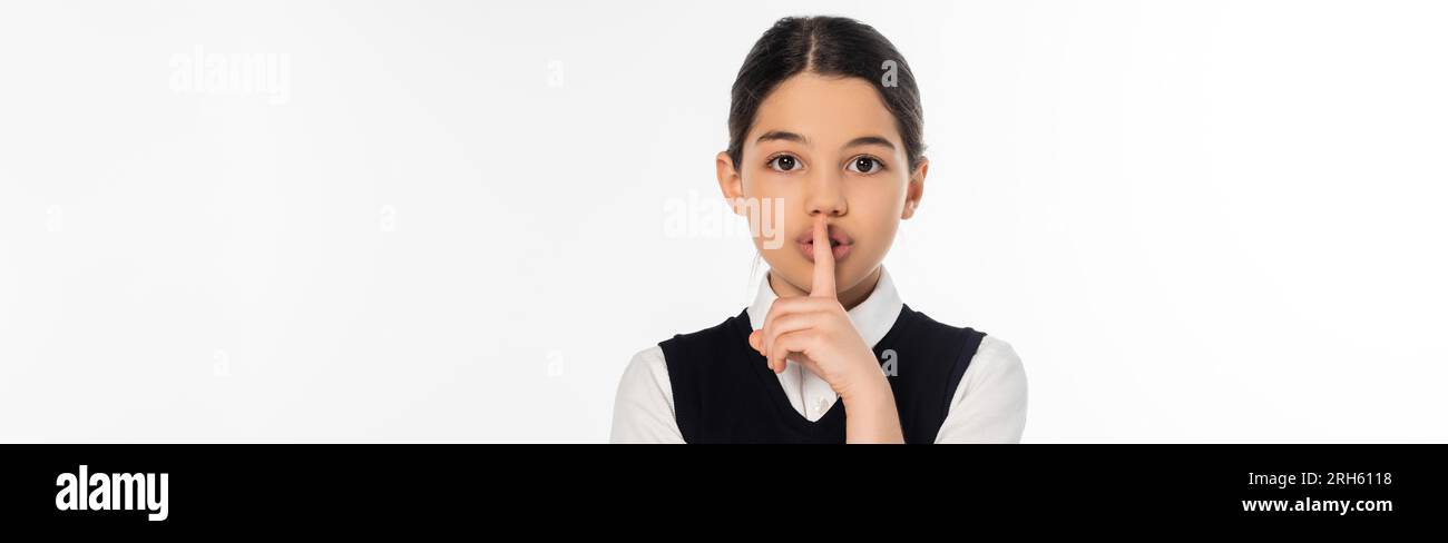 schoolgirl showing hush sign and looking at camera isolated on white ...