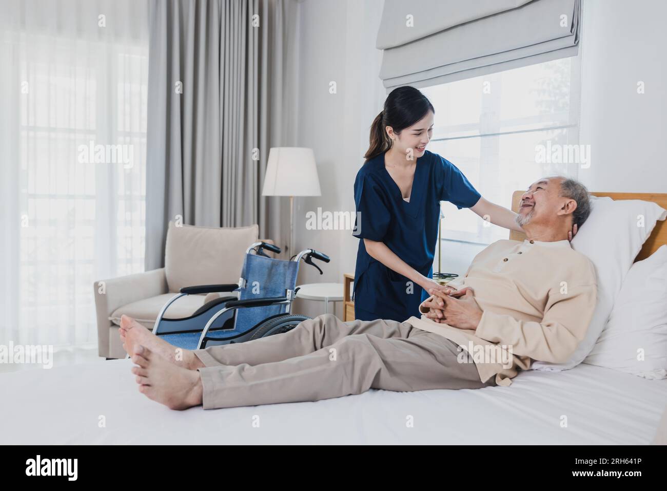 Senior Asian man laying on bed receives medical help for injury by Asian nurse, doctor woman ...