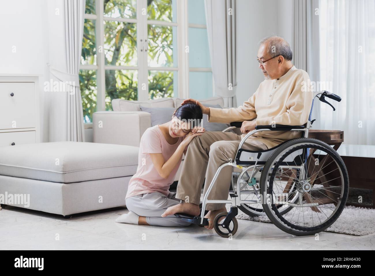 senior with beautiful daughter, old man sitting on wheelchair in house, caressing the head with ...