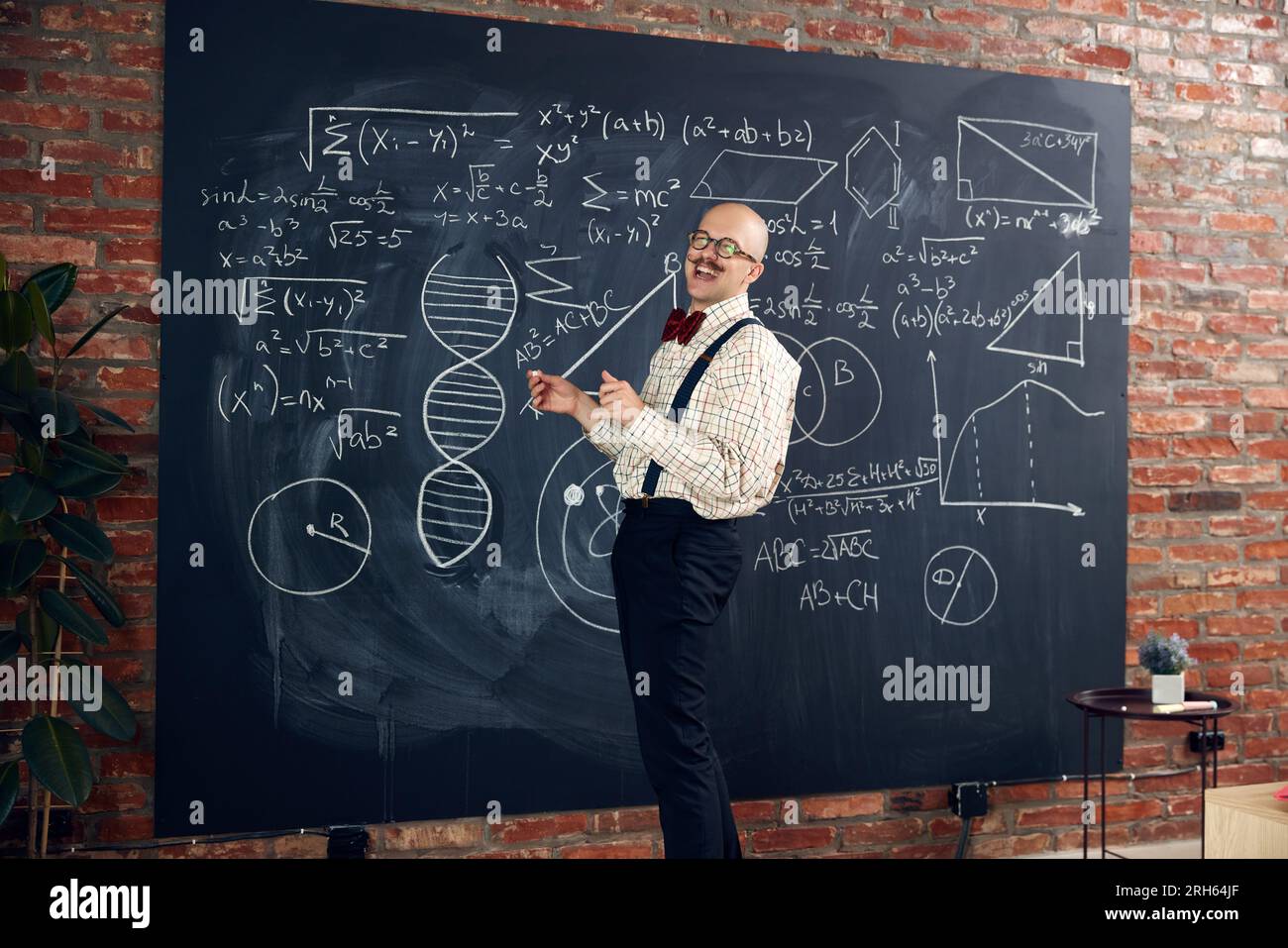 Young man, scientist, lecturer standing by blackboard with math and ...