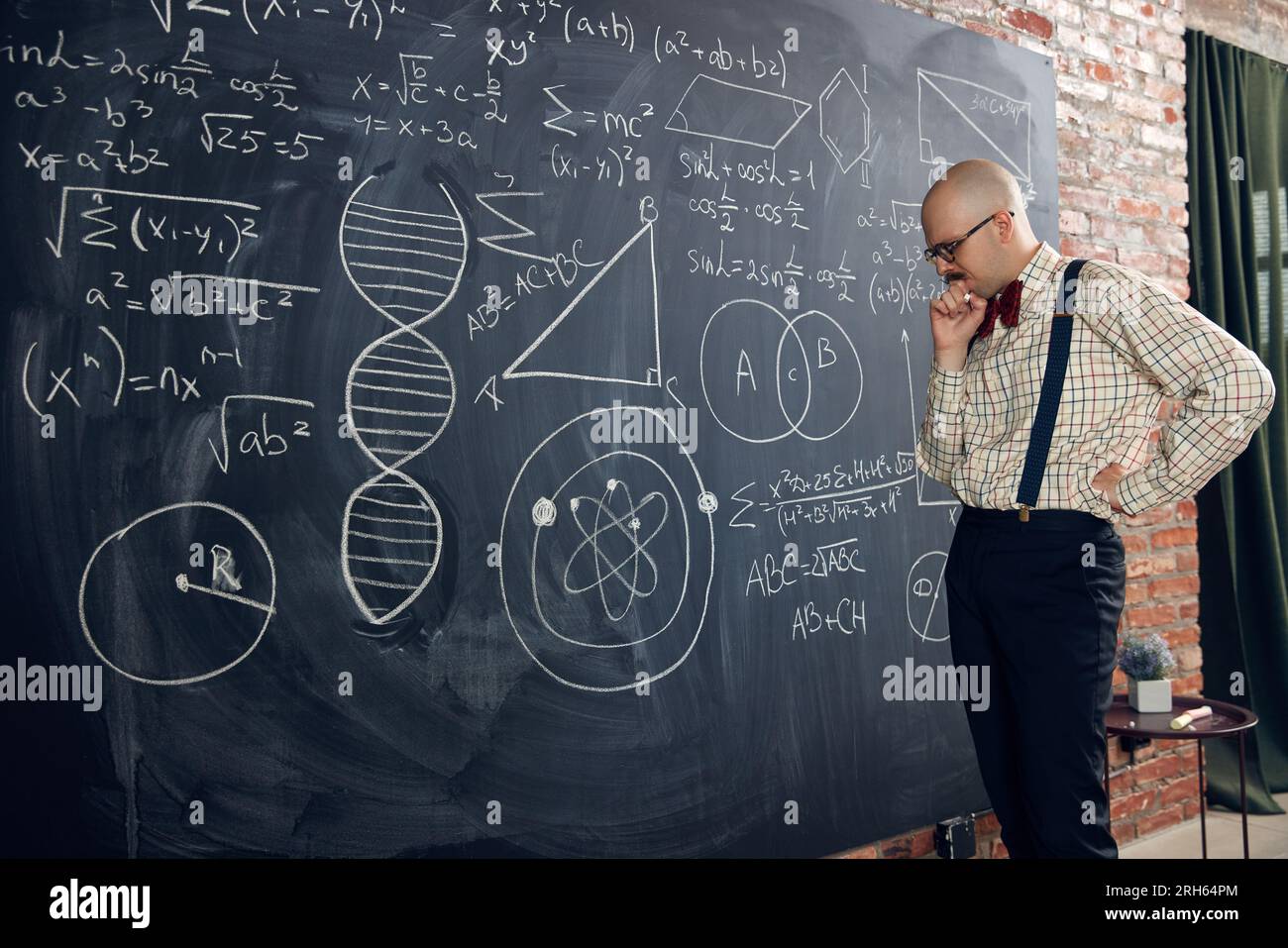 Young thoughtful man, scientist standing at blackboard with formulas ...