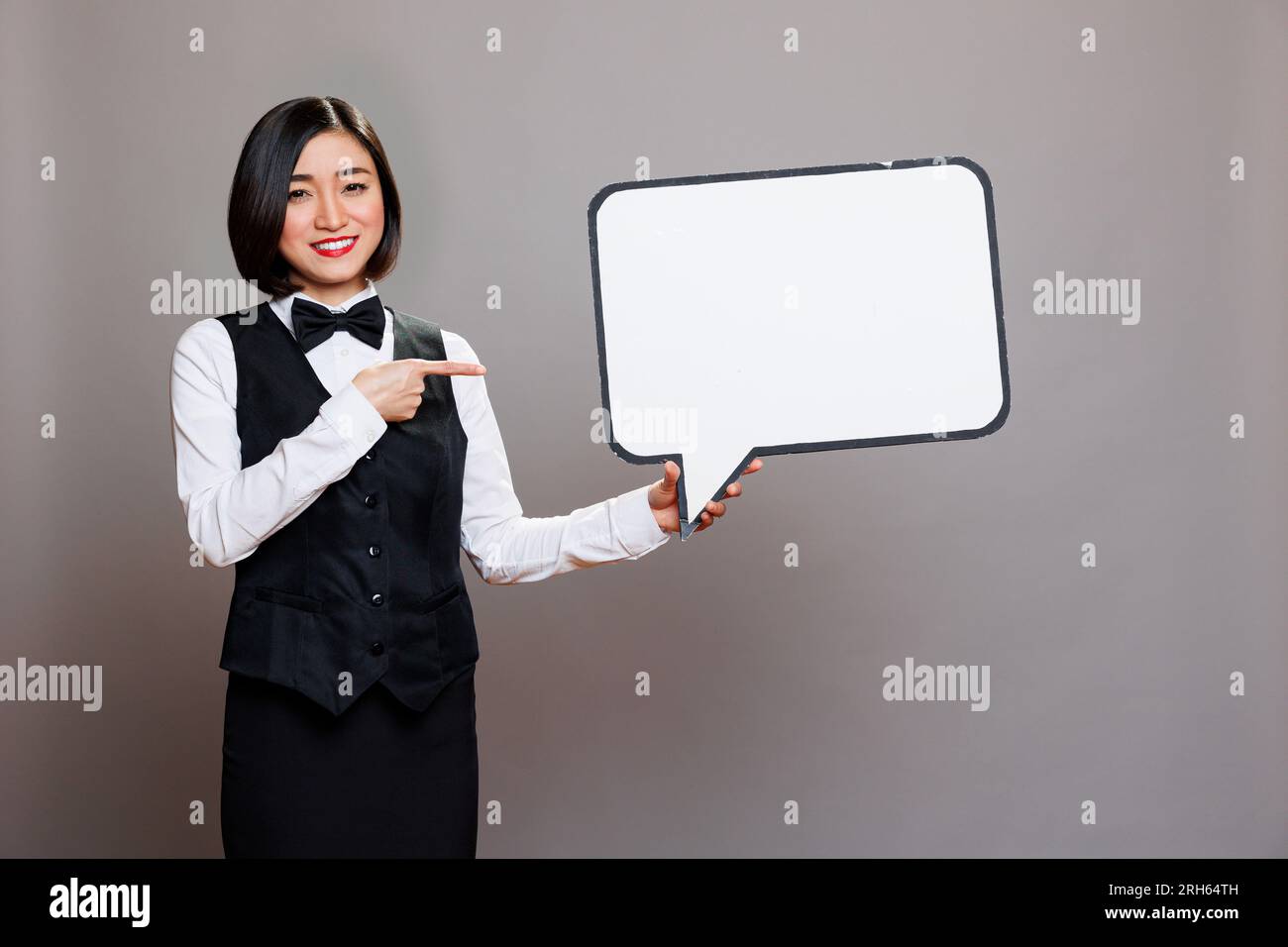 Smiling asian waitress in professional uniform holding speech cloud ...