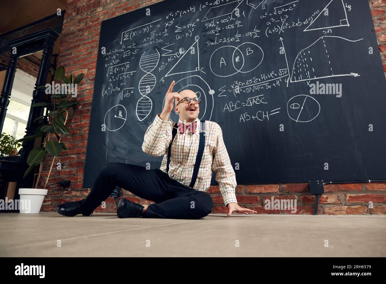 Young man, teacher, scientist sitting by blackboard with scientific ...