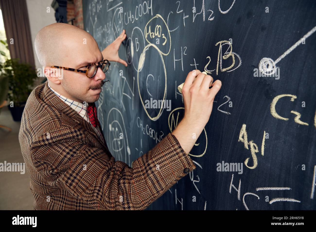 Young thoughtful man, scientist standing at blackboard with formulas ...