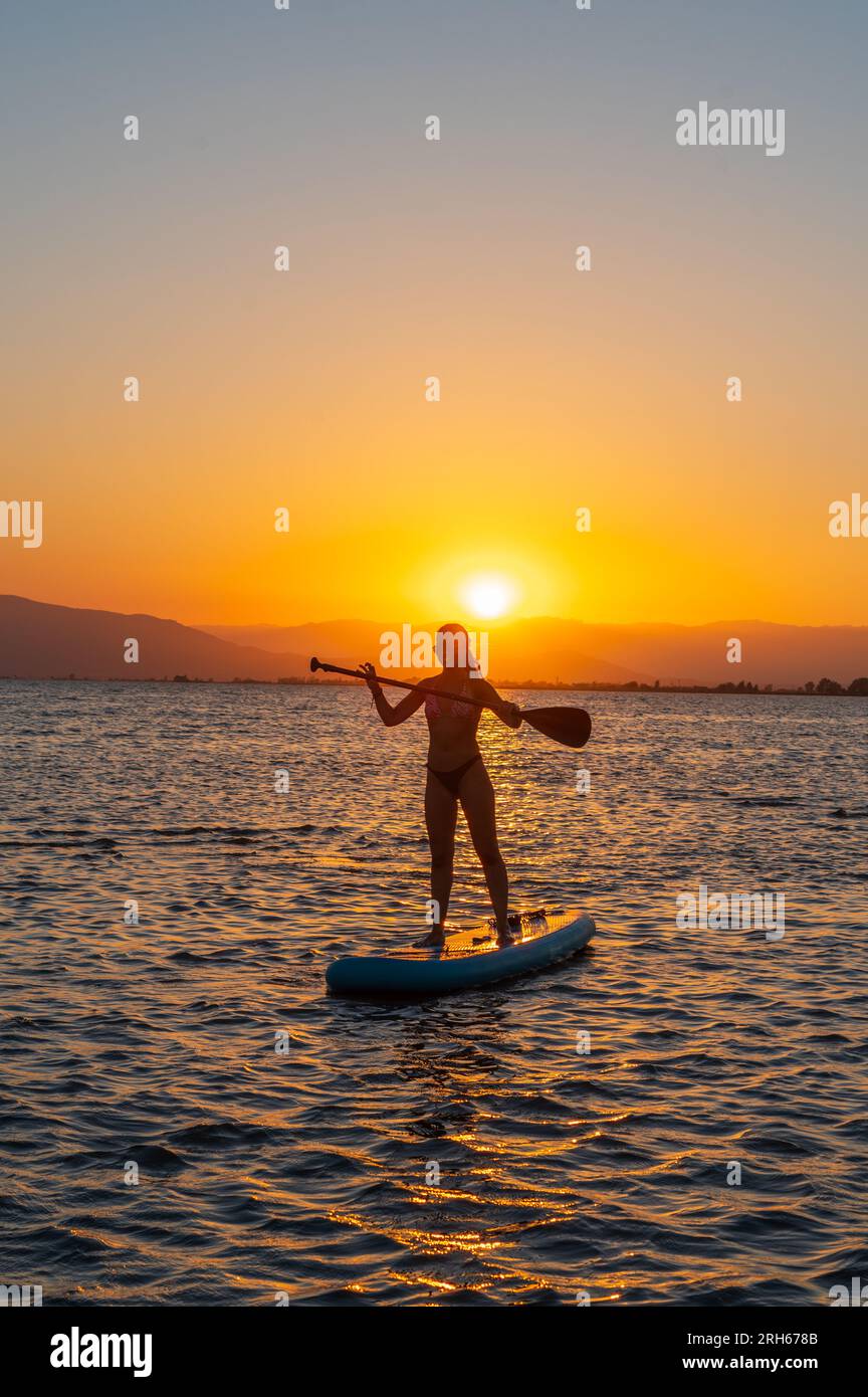 Silhouette of young woman practicing paddle surf during sunset at ...