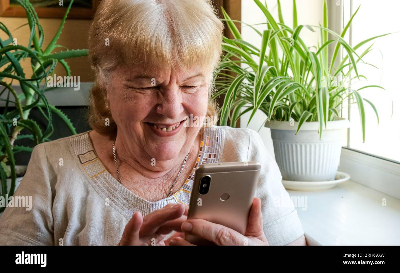 Happy smiling elderly woman using her phone at home. Grandma is typing ...